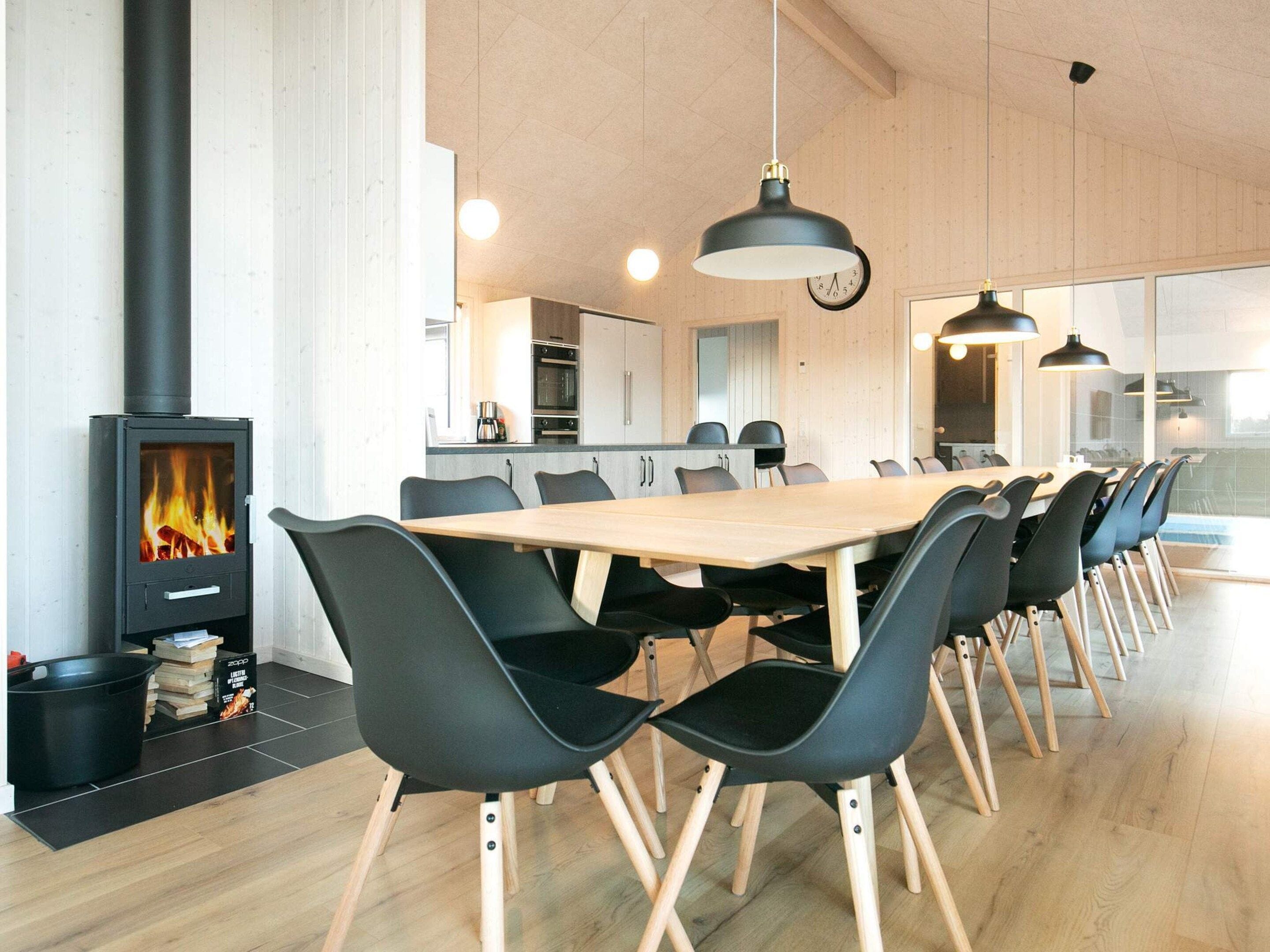 Uma cozinha moderna com lareira a lenha, área de jantar com mesa comprida e cadeiras, e iluminação pendente.