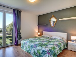 Quarto com cama grande, mesa de cabeceira, espelho e vista para o exterior.
