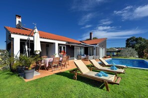 Uma casa moderna com telhado de telhas vermelhas, piscina e área de estar ao ar livre.