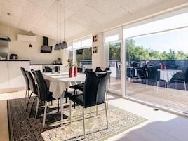 Uma sala de jantar moderna com uma mesa posta para quatro pessoas, cadeiras pretas e uma janela grande com vista para o exterior.