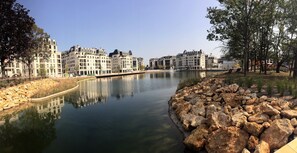 Um rio calmo com um aterro de pedra e árvores de um lado, e uma fileira de edifícios altos com varandas do outro.