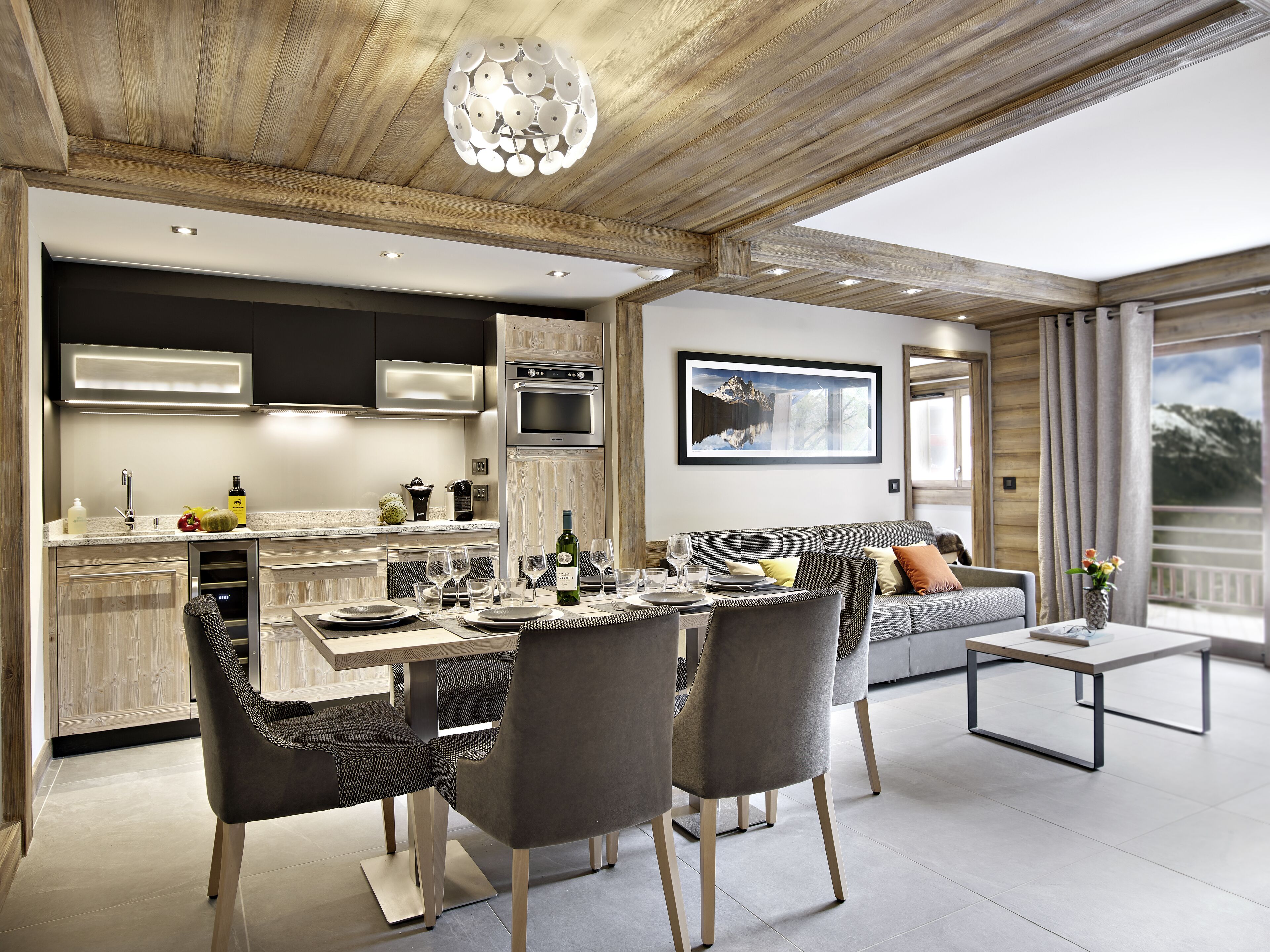 Uma cozinha moderna com eletrodomésticos embutidos, uma sala de jantar com mesa posta para quatro pessoas e uma sala de estar com sofá e mesa de centro.