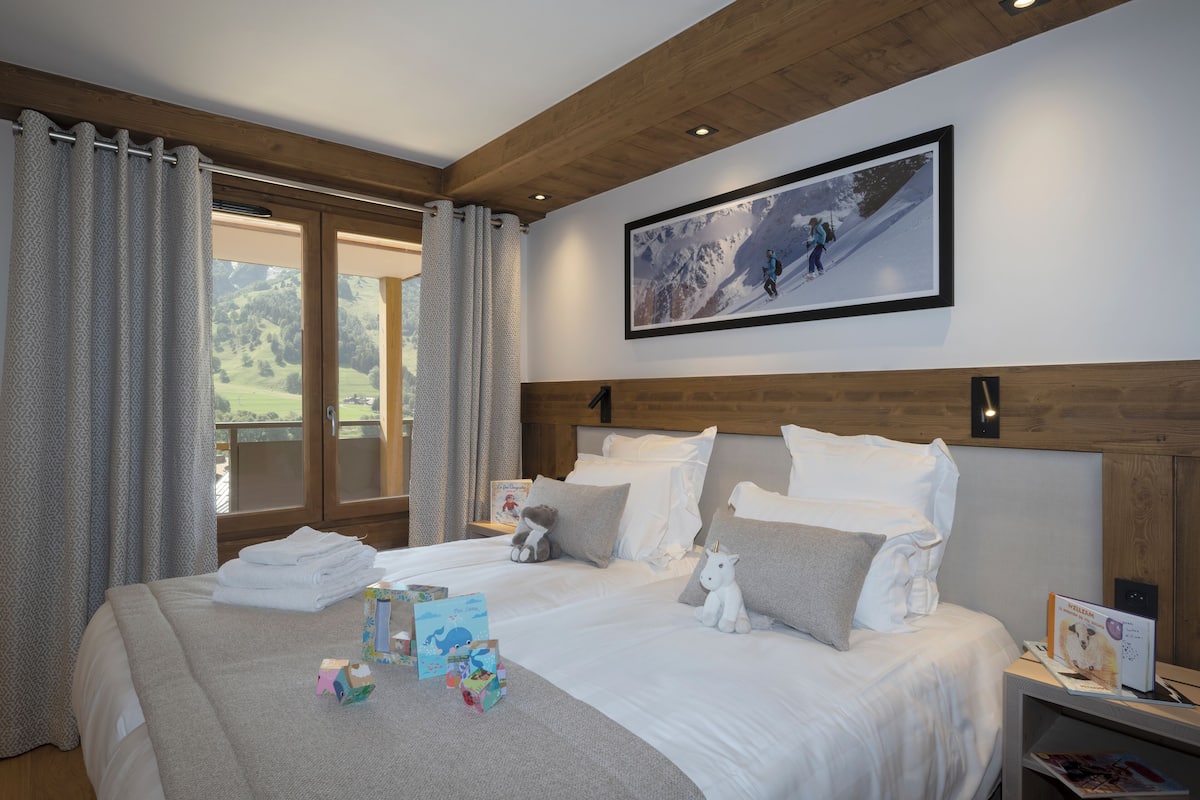 Quarto de hotel com uma cama grande, teto de madeira e vista para as montanhas pela janela.
