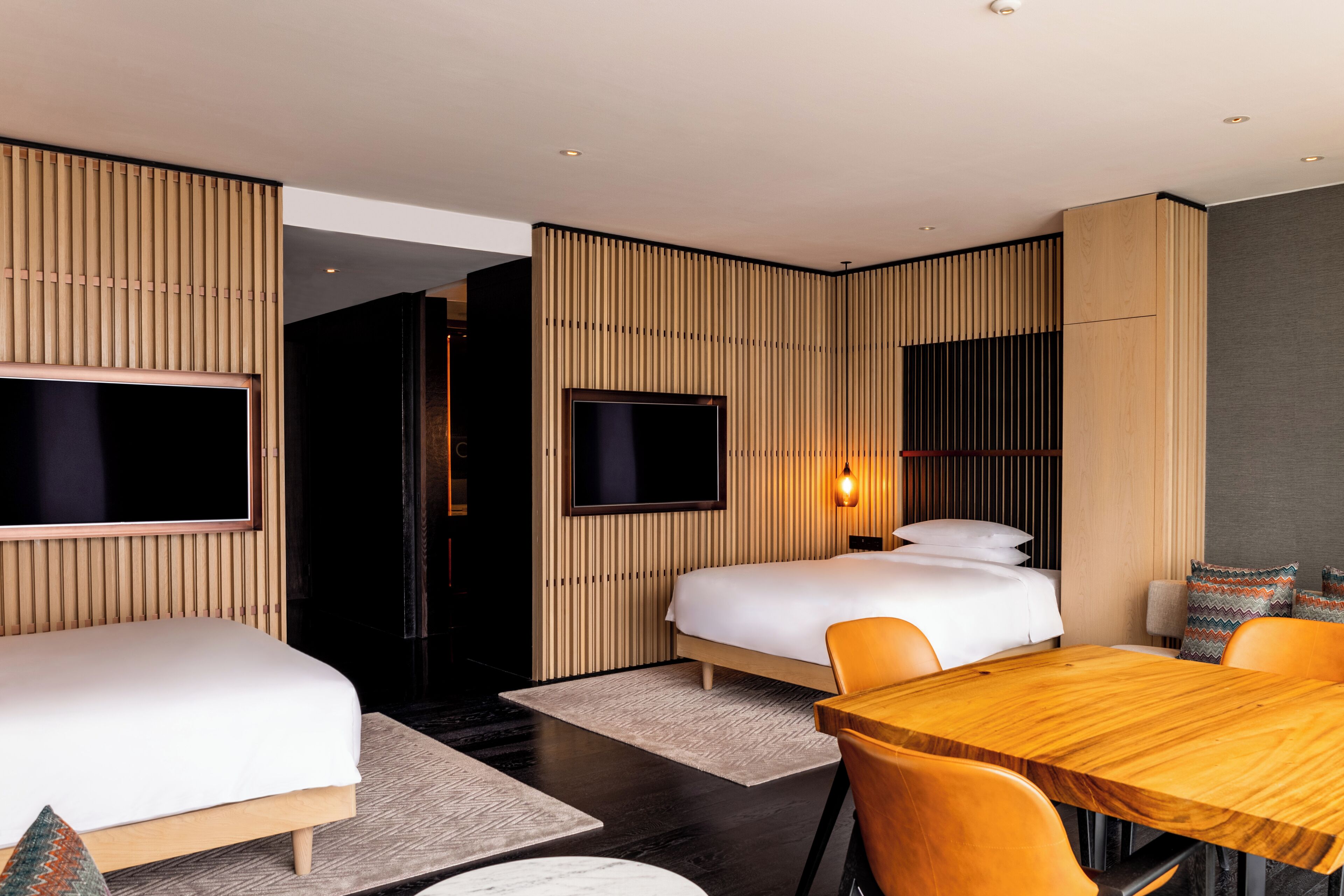 Quarto de hotel moderno com uma cama grande, televisão, mesa de jantar de madeira e área de estar separada.