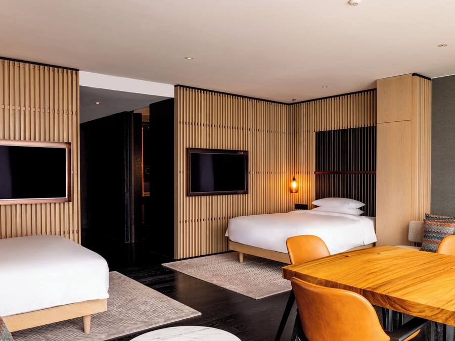 Quarto de hotel moderno com uma cama grande, televisão, mesa de jantar de madeira e área de estar separada.