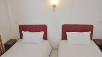 Duas camas de solteiro com cabeceiras vermelhas, roupa de cama branca e luminária fixada na parede.