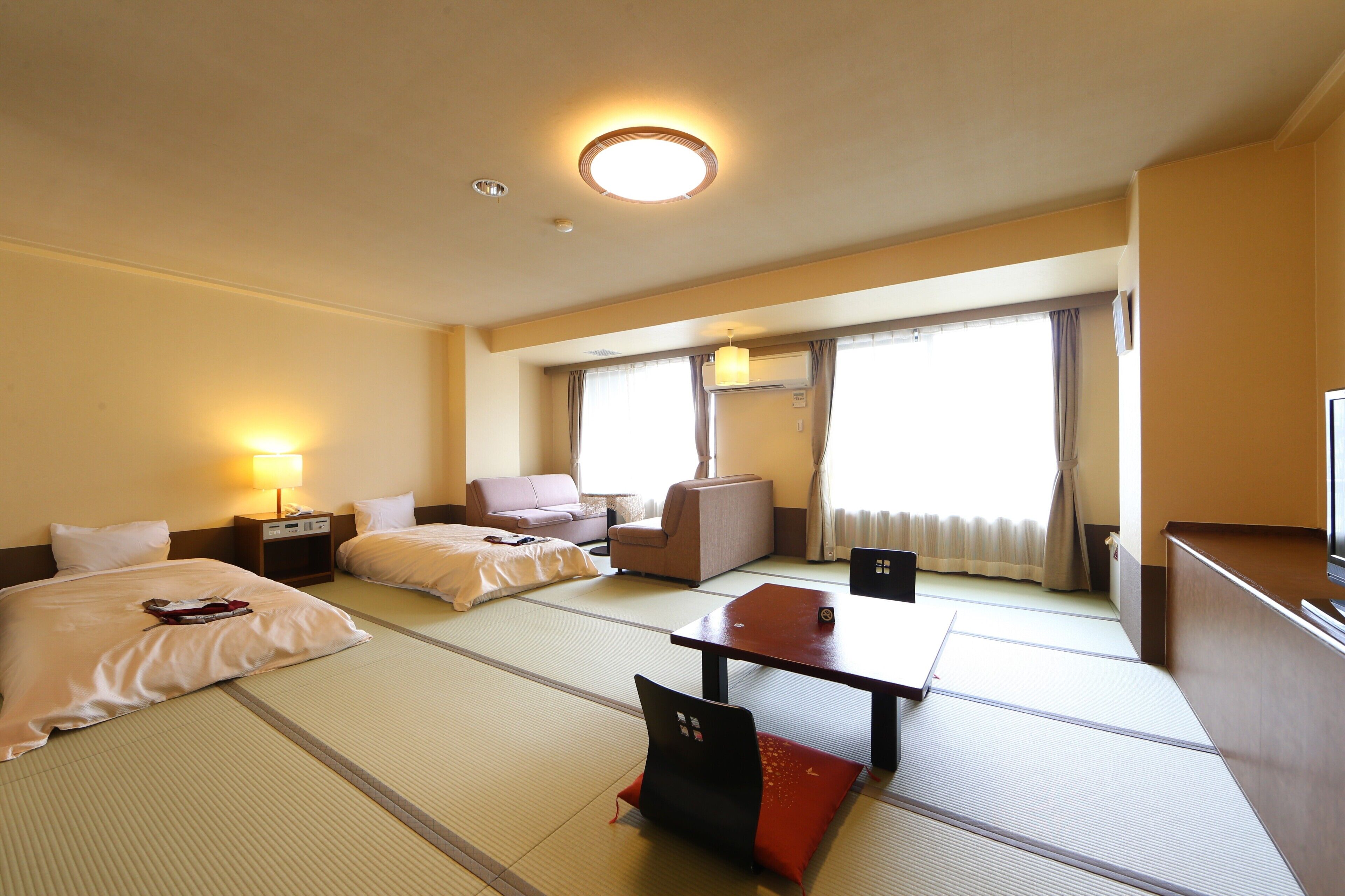 Quarto de hotel com piso de tatame, um sofá, uma mesa e uma televisão.