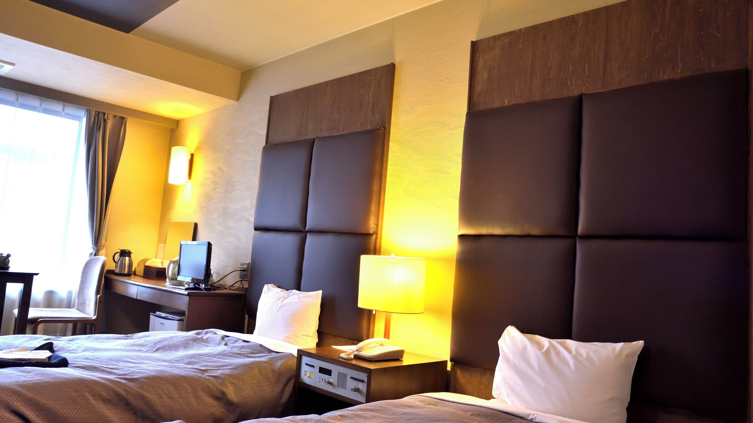 Quarto de hotel com uma cama grande, uma escrivaninha com computador, uma cadeira e uma luminária.