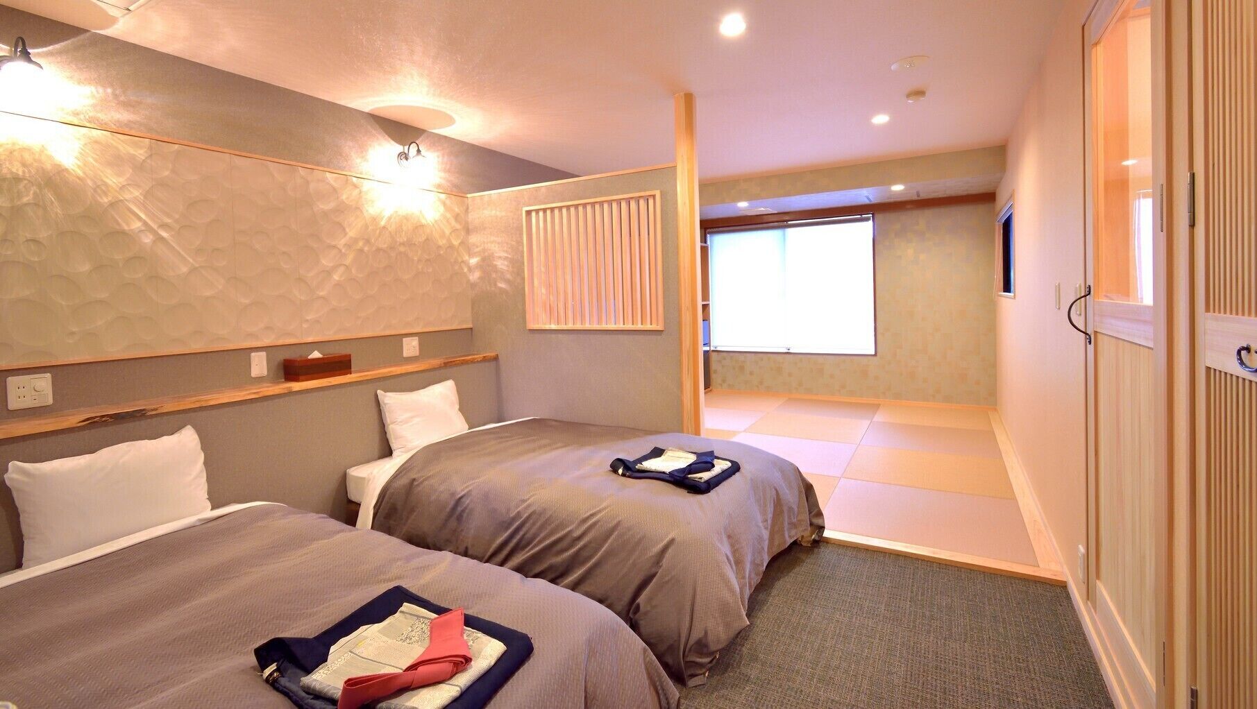 Quarto de hotel com duas camas, uma janela grande e um aplique na parede.