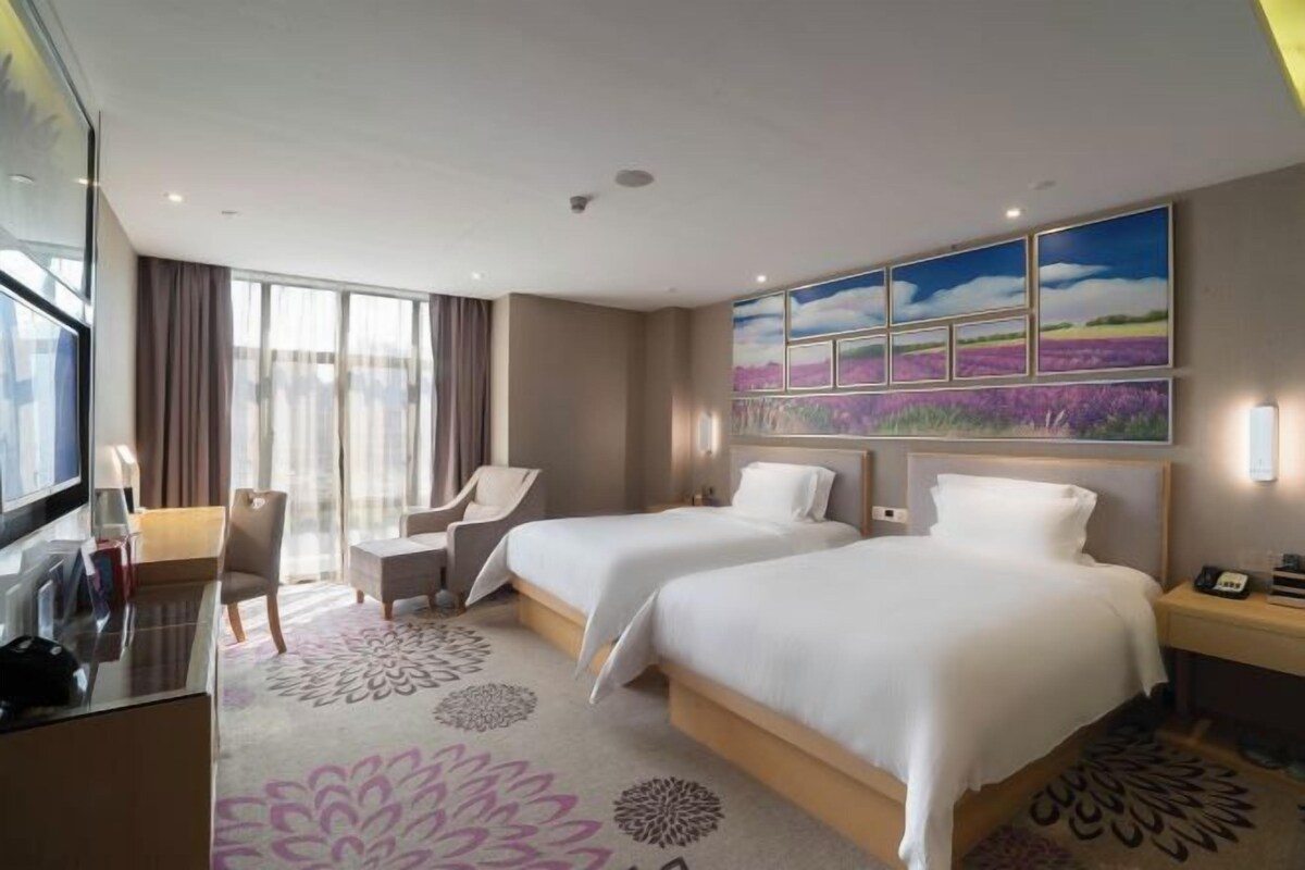 Quarto de hotel com duas camas, uma escrivaninha, uma cadeira, uma televisão e uma janela grande.