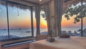 Quarto com uma grande janela com vista para o mar, uma cama e um pequeno espaço de estar.