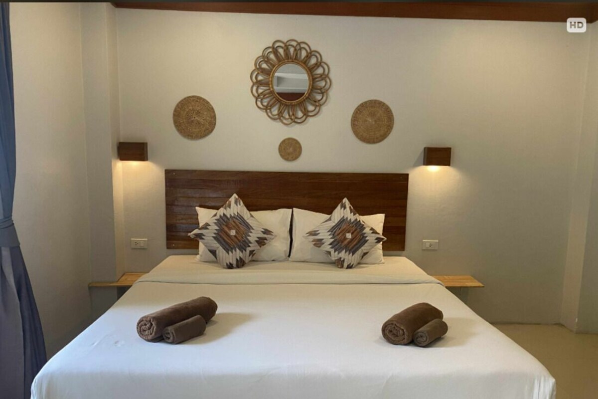 Cama bem arrumada com cabeceira de madeira, duas molduras de parede decorativas e um relógio de parede.