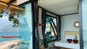 Quarto com uma grande janela com vista para uma praia e oceano.