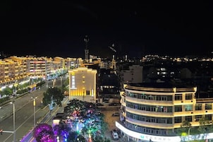 Um edifício de vários andares com fachada curva, pátio central e rua com árvores iluminadas.