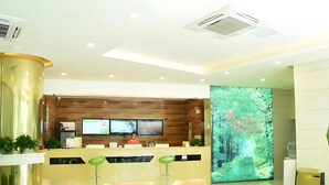 Uma área de recepção moderna com parede de madeira, uma tela digital exibindo uma floresta e um balcão de atendimento com duas cadeiras verdes.