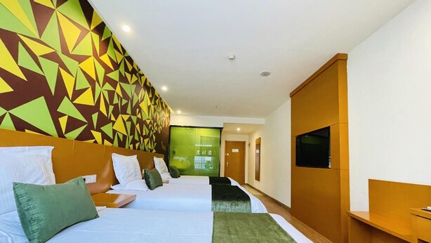 Quarto de hotel com três camas, carpete verde e parede com padrão geométrico.