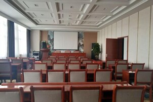 Uma sala de conferências com fileiras de cadeiras, uma tela de projeção e um pódio.