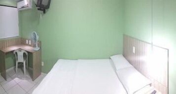 Quarto pequeno com uma cama de solteiro, escrivaninha e cadeira, ar-condicionado fixado na parede e uma janela.