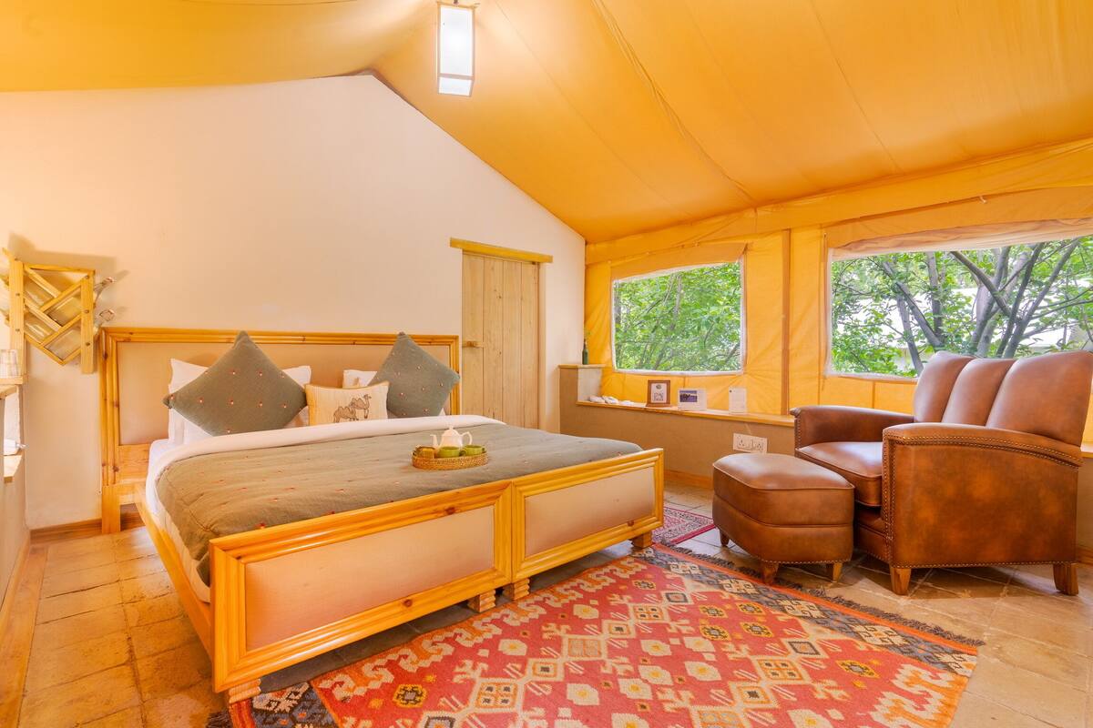 Um quarto aconchegante com uma cama de madeira, uma mesinha, uma cadeira e uma janela com vista para árvores.