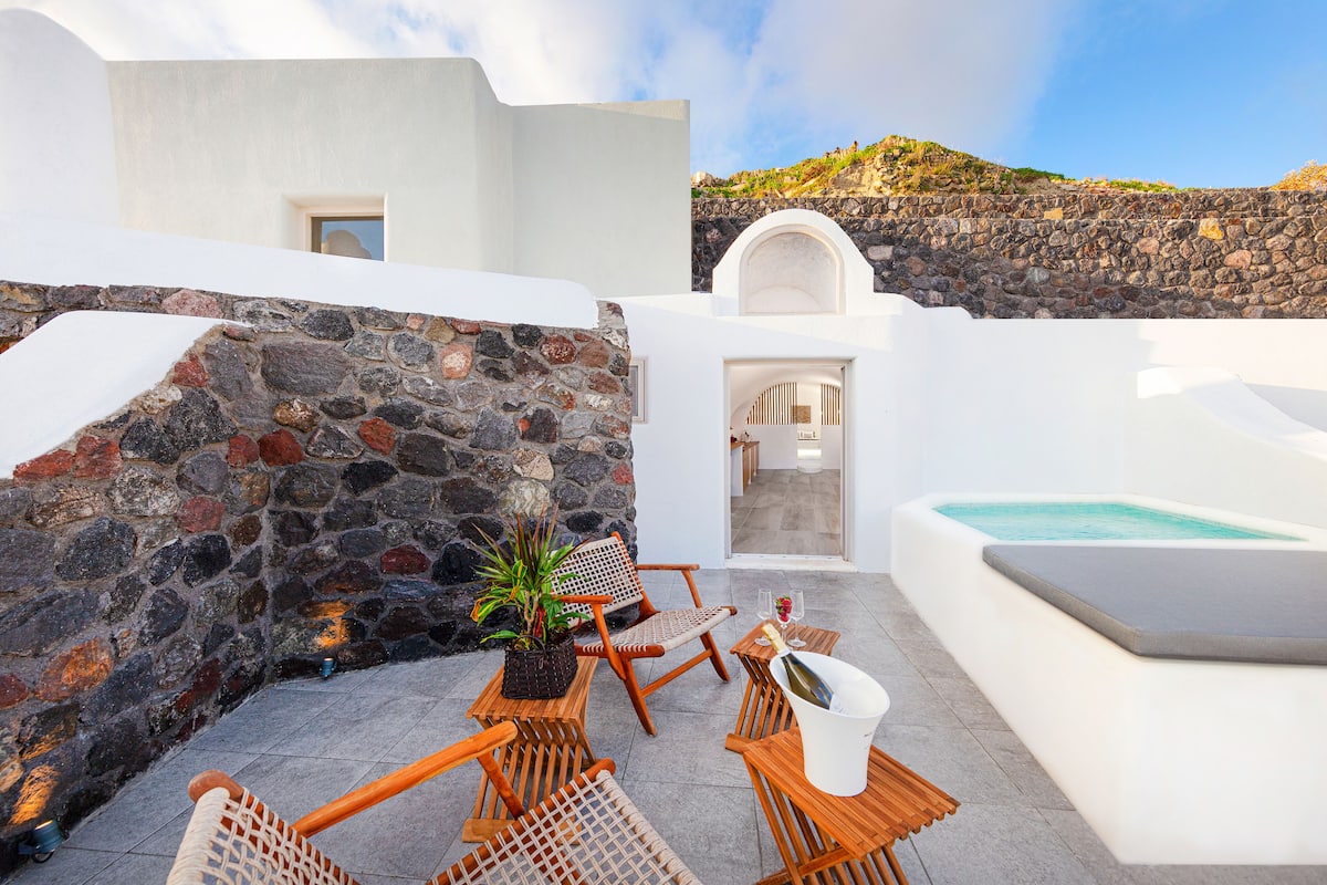 Um terraço no telhado com paredes de pedra, piscina, móveis de vime e vista para a paisagem.