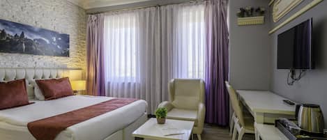 Quarto de hotel com uma cama, uma escrivaninha, uma cadeira, uma televisão e um quadro na parede.
