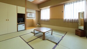 Um quarto japonês tradicional, com tatames, uma mesa de madeira baixa, uma televisão e um frigorífico pequeno.