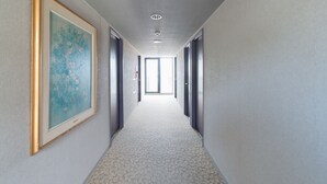 Um corredor comprido e estreito com carpete estampado, obras de arte emolduradas na parede à esquerda e portas nos dois lados que dão para os quartos.