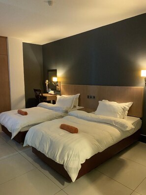 Quarto de hotel com duas camas, uma cabeceira de madeira, uma mesa de cabeceira e um espelho.