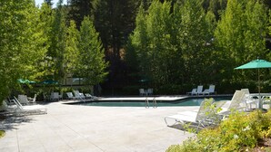 Uma piscina com espreguiçadeiras e guarda-sóis, cercada por árvores.