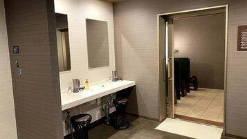 Uma casa de banho moderna com uma pia branca, dois taburetes pretos, um espelho e uma porta que dá para um espaço sanitário.
