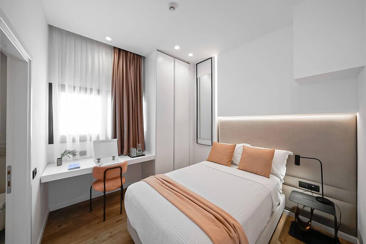Quarto de hotel moderno com cama, escrivaninha, cadeira e um espelho grande.