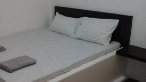 Uma cama de solteiro com roupa de cama e almofadas brancas, cabeceira escura e mesa de cabeceira pequena com uma toalha.