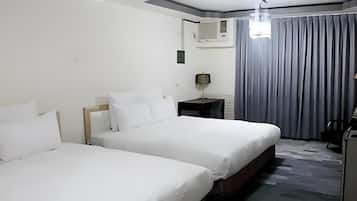 Quarto de hotel com duas camas, uma escrivaninha, uma luminária e vista para o exterior.