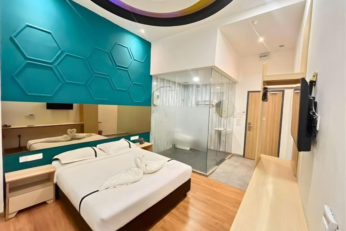Quarto de hotel moderno com cama grande, box de chuveiro em vidro e parede decorada em tons de verde-água.
