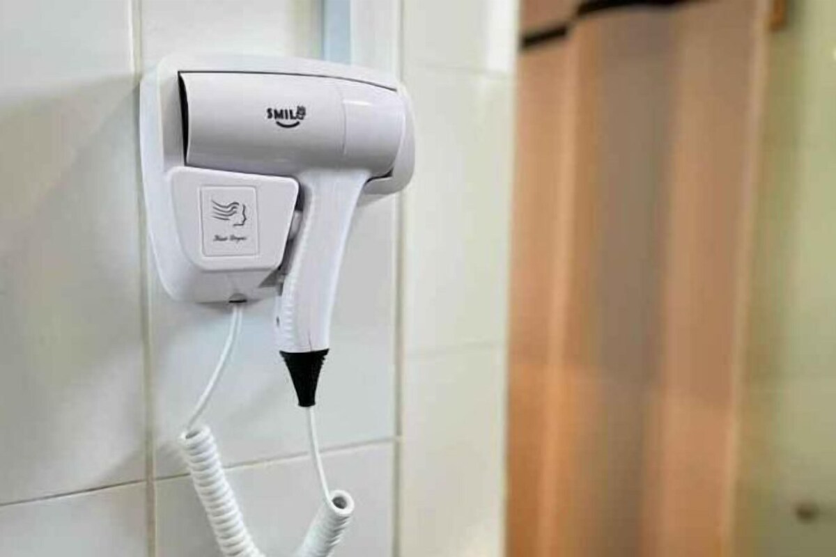 Secador de cabelo fixado na parede, com cordão, tomada e botão de controle.