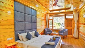 Quarto de cabana de madeira com uma cama, duas cadeiras, uma mesinha e uma janela.