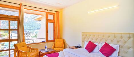 Quarto de hotel com cama, poltrona, mesinha e janela com cortinas.
