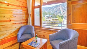 Quarto de cabana de madeira com duas cadeiras, uma mesa e janela com vista para as montanhas.
