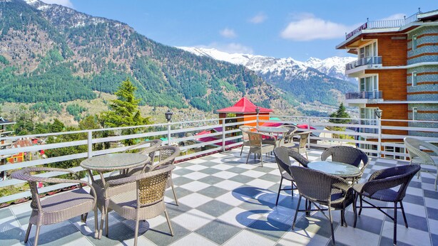 Terraço com mobiliário de vime e piso xadrez, com vista para uma paisagem montanhosa com picos nevados.