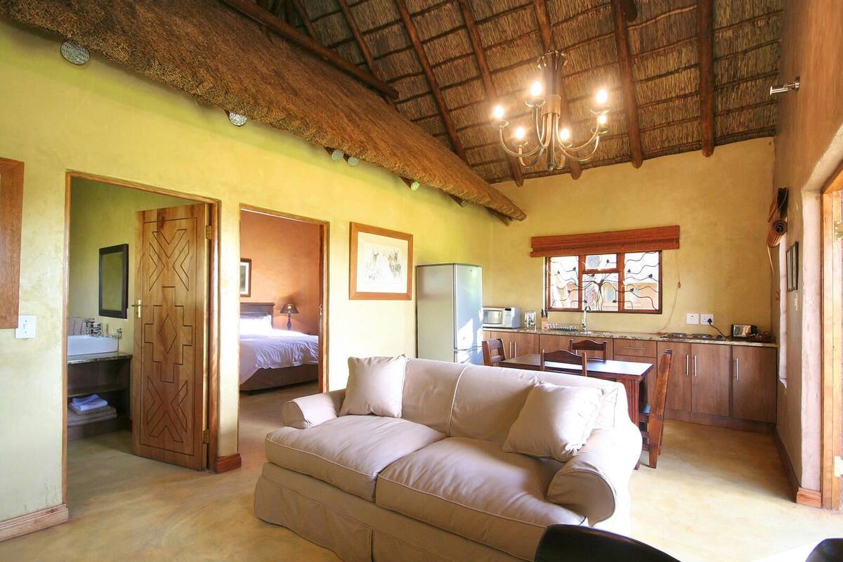 Quarto com um amplo sofá bege, cama, cozinha compacta e área de jantar.