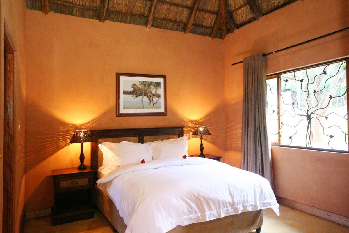 Quarto com cama, duas mesas de cabeceira, um quadro na parede e janela com cortinas.