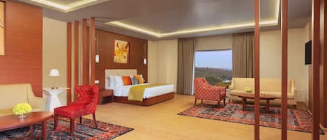 Quarto de hotel com uma cama, duas áreas de estar, uma TV e vista para o exterior.