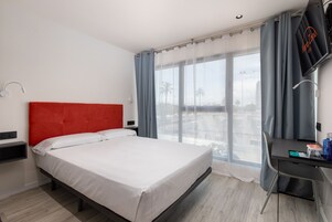 Quarto de hotel com cama, escrivaninha, televisão e janela com cortinas.
