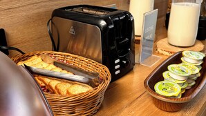 Disposição de buffet de café da manhã com torradeira, cesta de torradas, dispensador de leite e potes de iogurte.