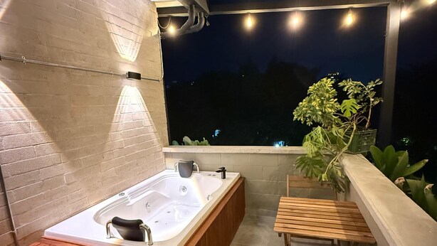 Um banheiro externo moderno com hidromassagem, bancos de madeira e luzes de fada.