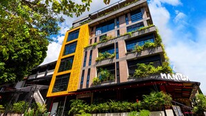 Um hotel de vários andares com design moderno, apresentando varandas com vegetação, grandes janelas e um letreiro chamativo para o restaurante.