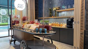 Um carrinho de comida com lanches e bebidas, um anúncio de Coca-Cola e uma placa com a inscrição "Mini Mart" em um interior moderno com paredes azulejadas e vista para a piscina.