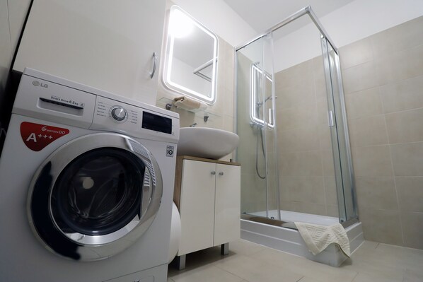 Uma casa de banho moderna com máquina de lavar, cabine de duche em vidro e lavatório branco.