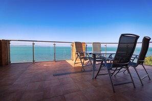 Varanda com vista para o mar, uma mesa com cadeiras e guarda-corpo de vidro.
