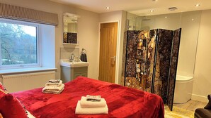 Quarto de hotel com uma cama grande, janela, banheiro com chuveiro e espelho.